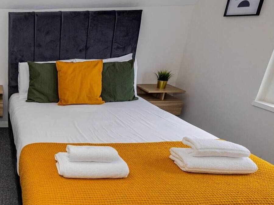 Quarto de hotel com cama, mesa de cabeceira, planta em vaso e quadro pendurado na parede.