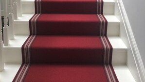 Uma escadaria com tapete vermelho e balaústres brancos.