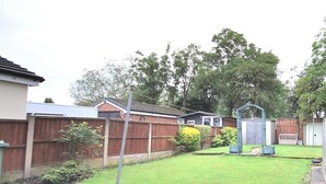 Quintal residencial com gramado, cerca de madeira, um galpão e uma pequena área de jardim com plantas.