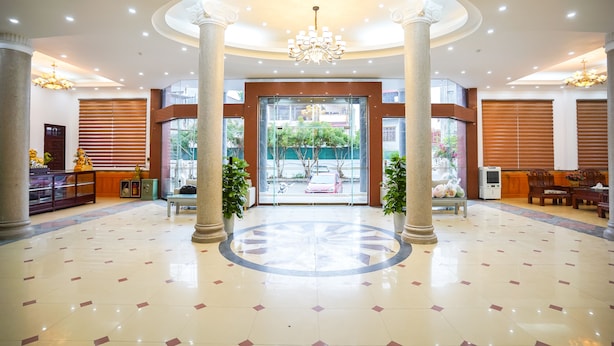 Um hall amplo com design circular no chão, colunas imponentes e um lustre.