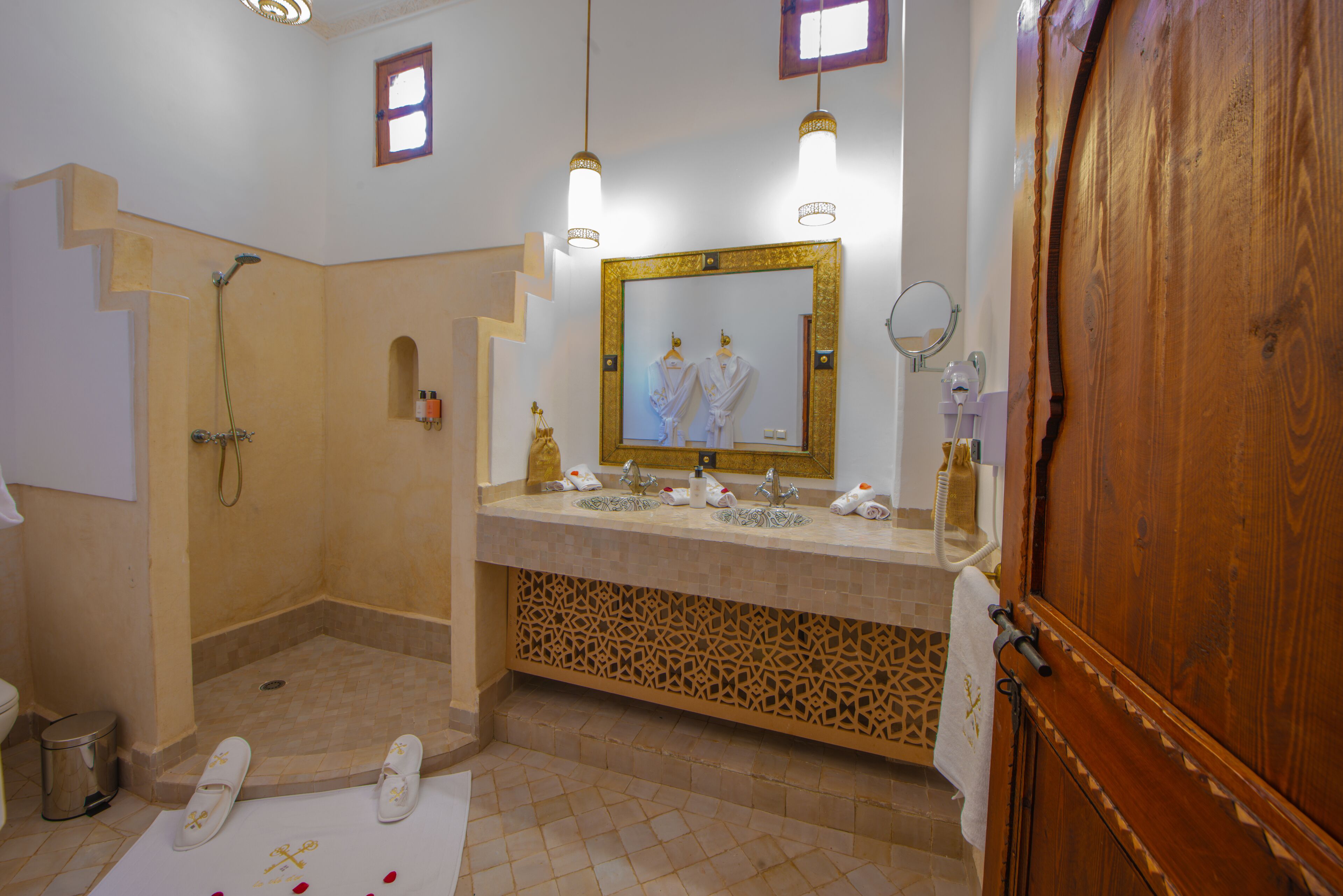 Casa de banho com chuveiro, duas pias, um espelho e uma porta de madeira.