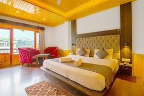 Quarto de hotel com uma cama grande, cadeiras vermelhas, uma mesa pequena e vista pela janela.