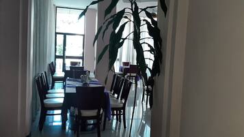 Uma sala de jantar com uma mesa posta para quatro, cadeiras e uma grande planta em vaso.