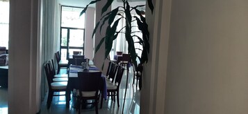 Uma sala de jantar com uma mesa posta para quatro, cadeiras e uma grande planta em vaso.