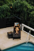 Uma pessoa relaxando em uma espreguiçadeira perto de uma piscina, lendo um livro.