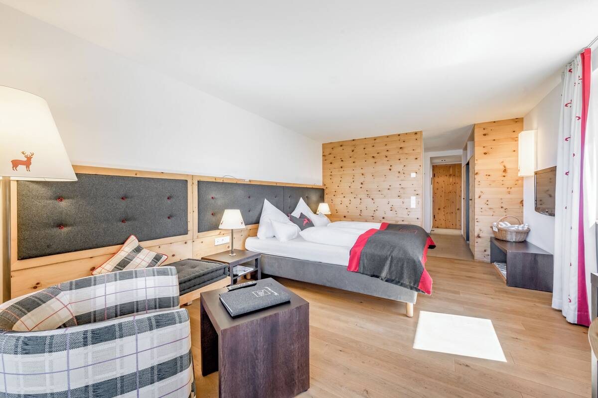 Quarto de hotel moderno com uma cama grande, cabeceira de madeira, uma pequena mesa e uma cadeira.