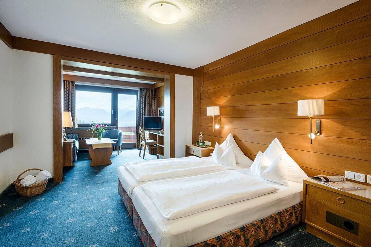 Quarto de hotel com duas camas, uma escrivaninha, uma cadeira, uma televisão e janela com vista.