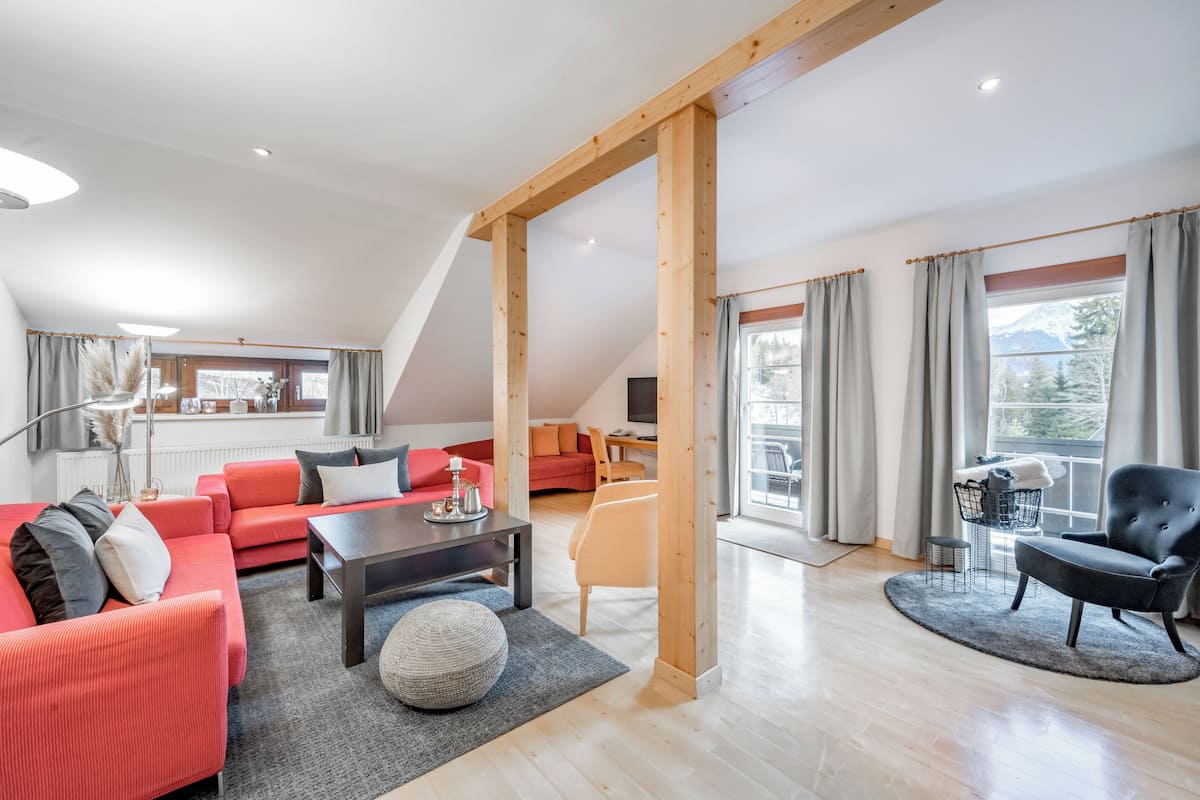 Uma sala de estar moderna com um sofá vermelho, uma poltrona preta e estrutura de teto em madeira.