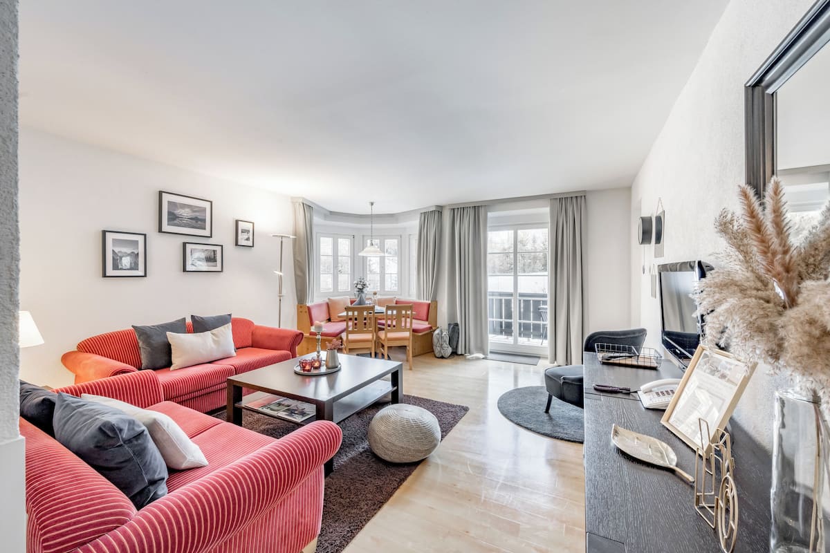 Uma sala de estar moderna com sofás vermelhos, uma mesa de centro e uma área de jantar com um candelabro.