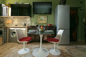 Uma cozinha compacta com máquina de lavar, geladeira, mesa de jantar com duas cadeiras e televisão fixada na parede.