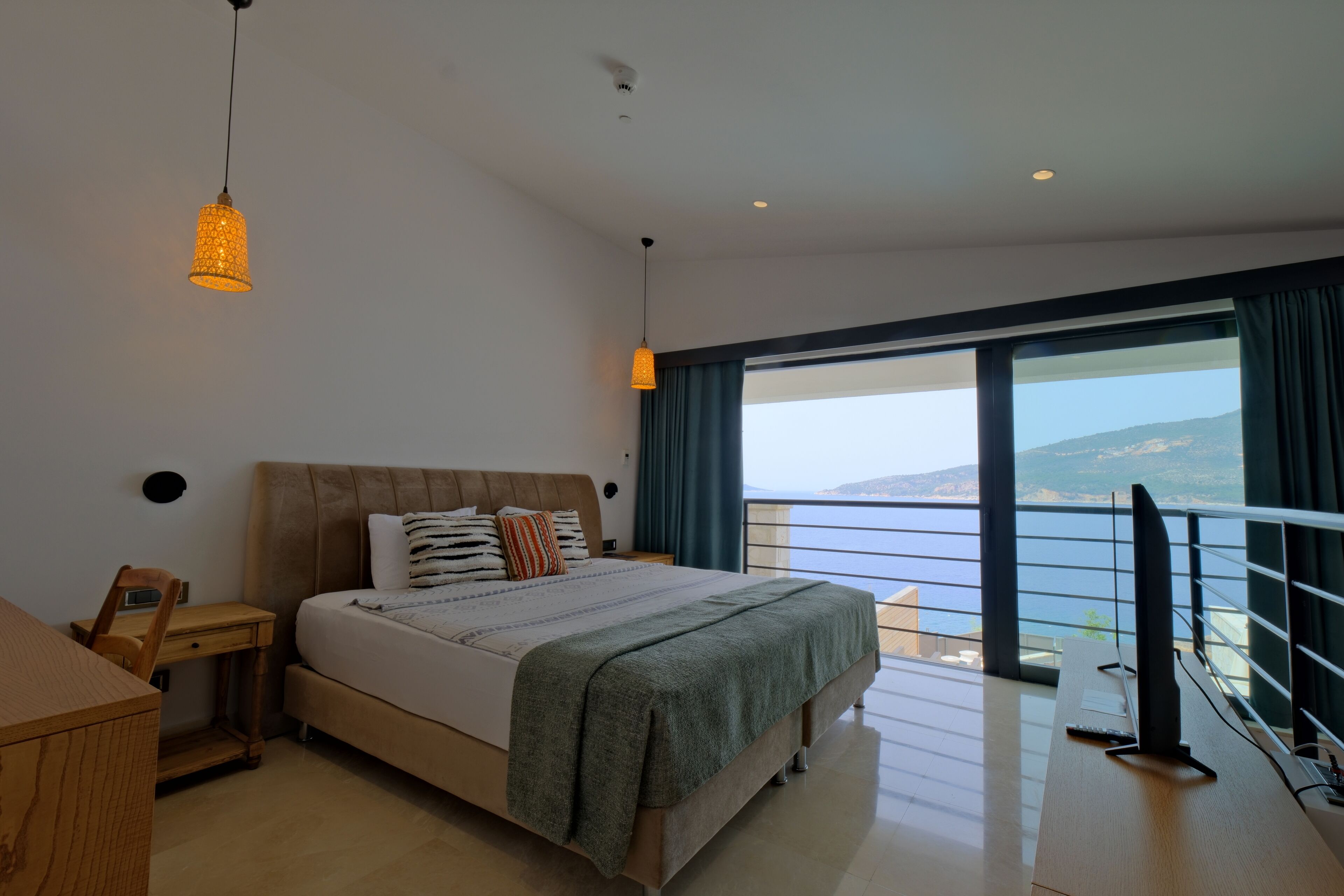 Quarto moderno com uma cama grande, uma escrivaninha e vista para o mar.