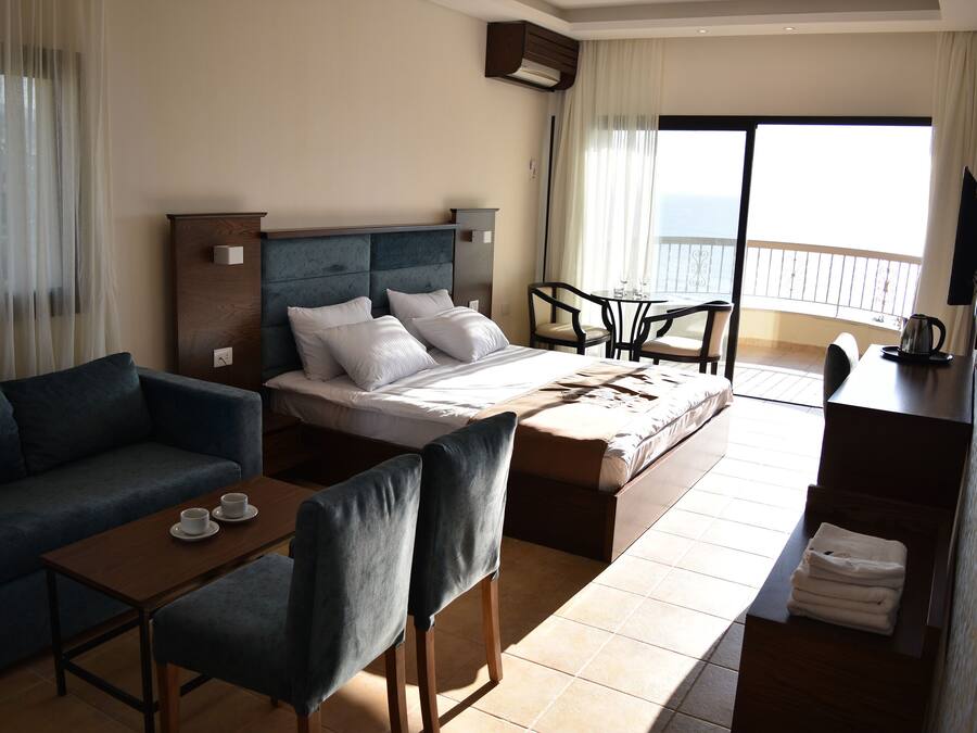 Quarto de hotel com cama, sofá, escrivaninha e varanda com vista.