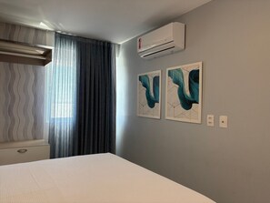 Quarto de hotel com cama, ar condicionado, cortinas e duas pinturas abstratas na parede.