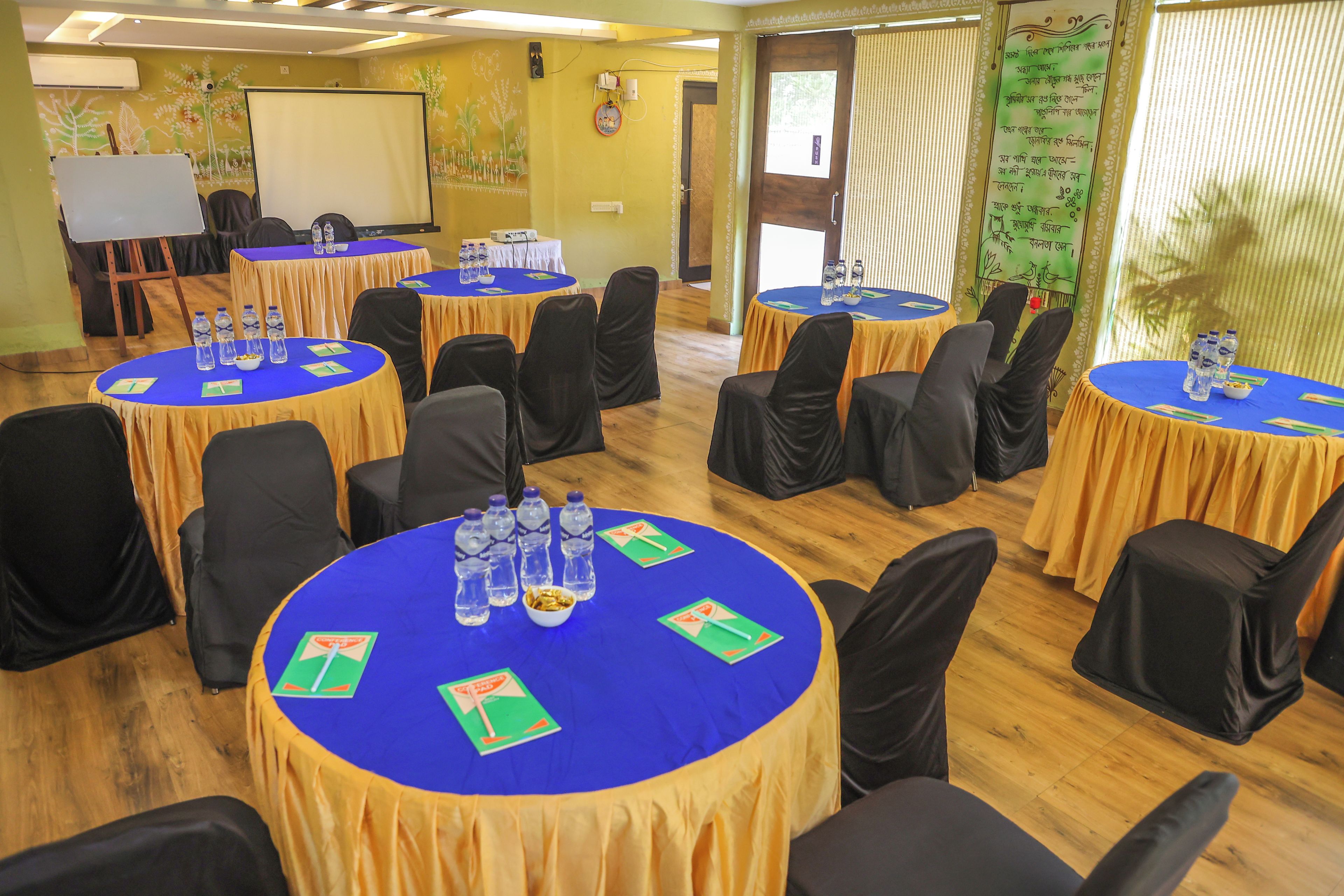 Sala de conferências com mesas redondas, cadeiras pretas e toalhas de mesa azuis.