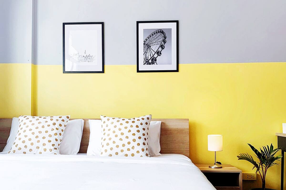 Quarto de hotel com cama, duas mesas de cabeceira, abajur e planta em vaso.