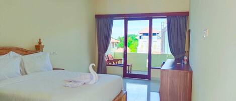 Quarto de hotel com cama, cabeceira de madeira, escrivaninha e vista para o exterior.