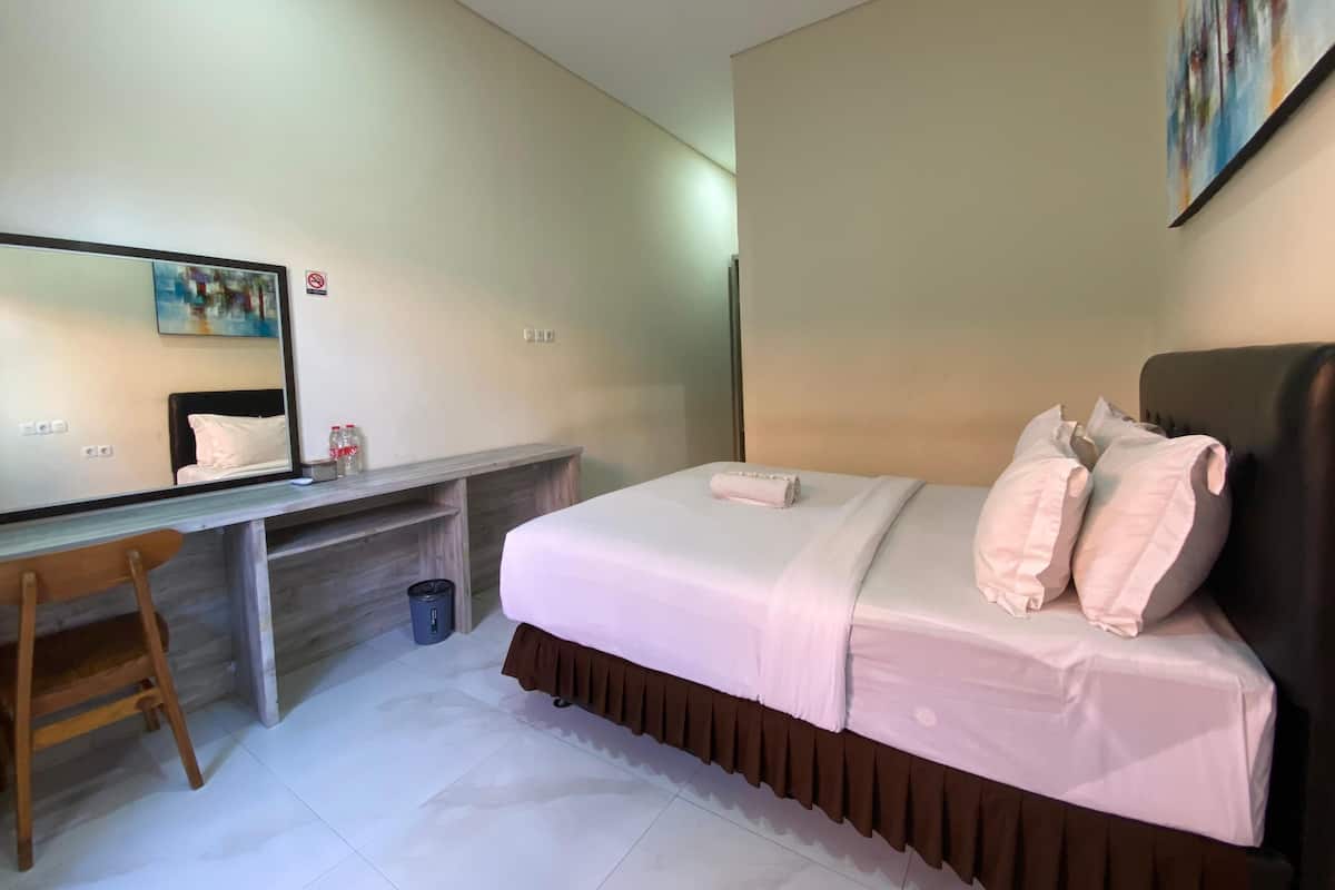 Quarto de hotel com cama, escrivaninha, cadeira, lixeira e um quadro na parede.