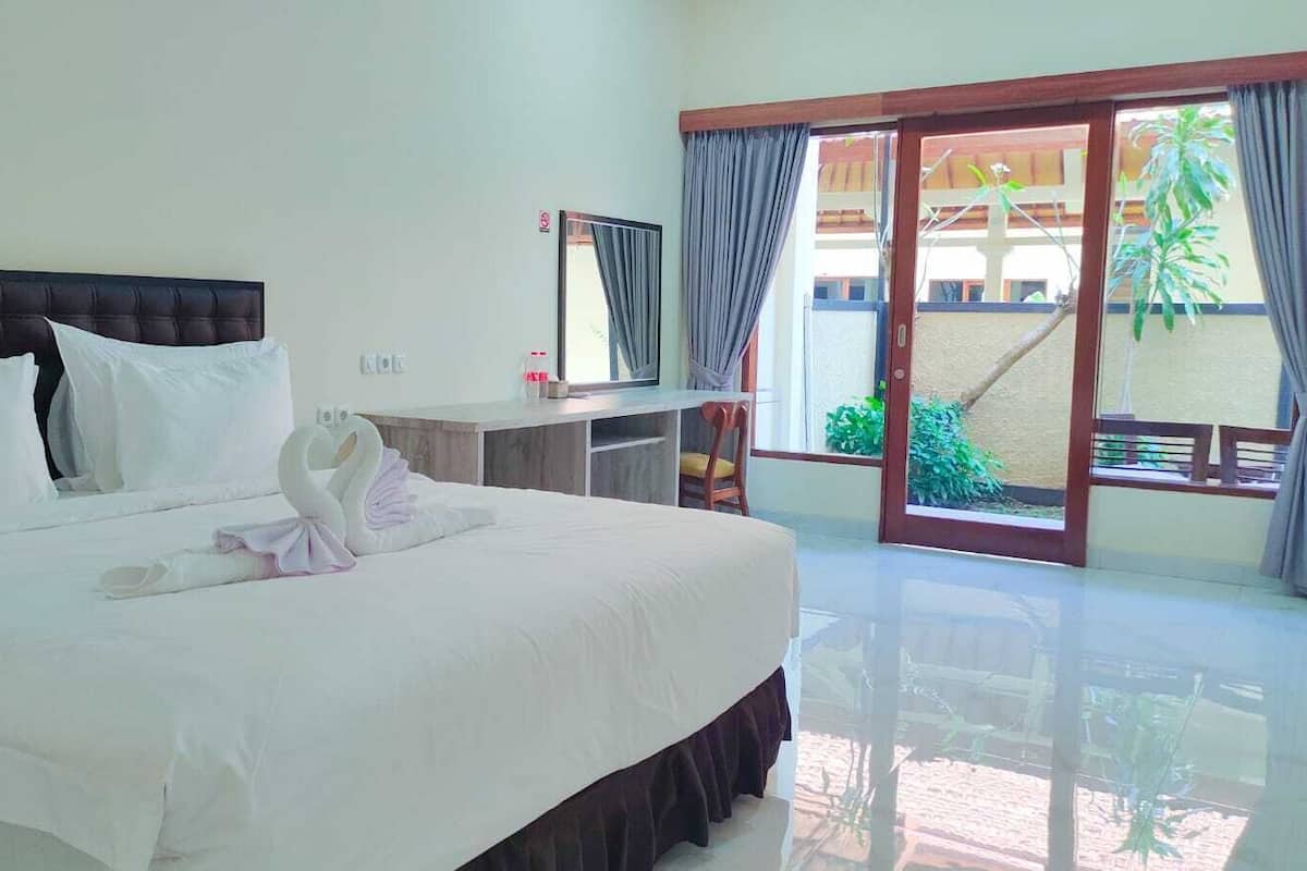 Quarto de hotel com uma cama grande, uma escrivaninha e uma varanda com cortinas.