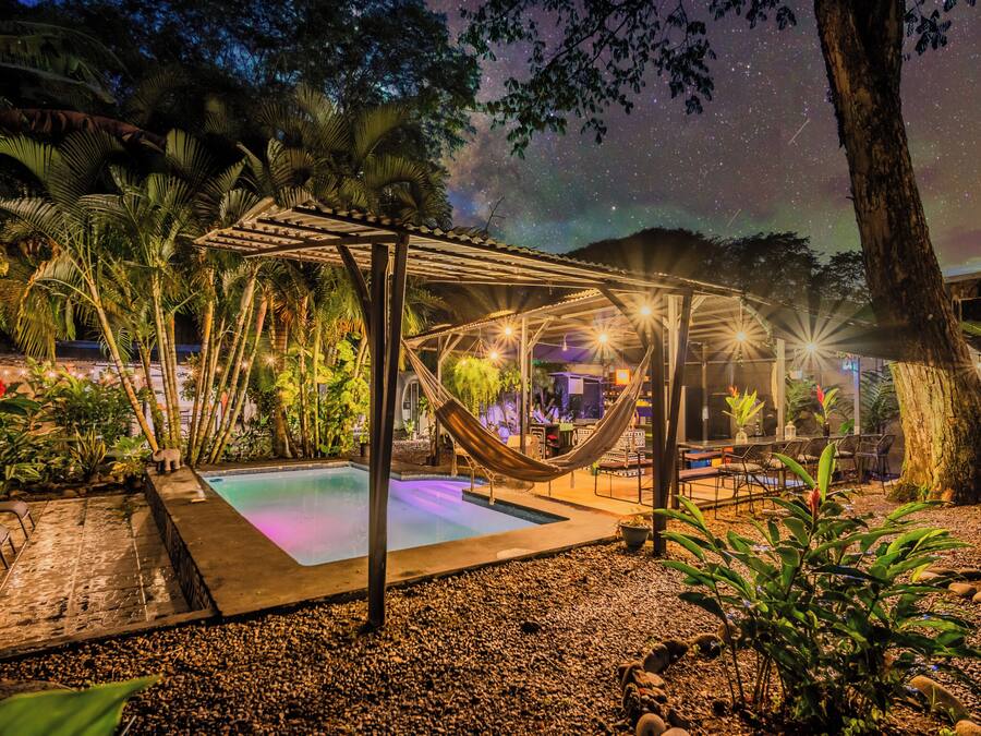 Área de piscina ao ar livre à noite, com rede, assentos e uma estrutura coberta.