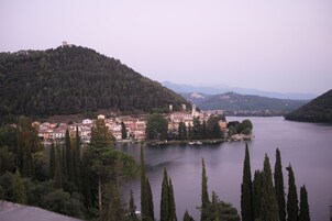 Uma cidade à beira de um lago, com edifícios ao longo da margem, um castelo no topo de uma colina e uma floresta densa em primeiro plano.