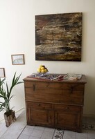 Um armário de madeira com uma tigela de limões em cima, uma planta em vaso e um quadro na parede.