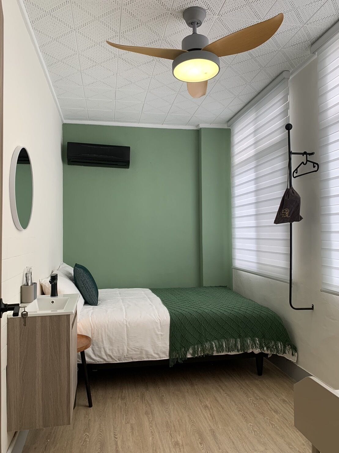 Quarto com cama, ventilador de teto, janela com persianas, mesa de cabeceira e luminária suspensa.