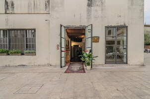 Entrada de um edifício com fachada de concreto, porta de vidro e um vaso de planta.