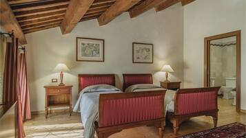 Quarto com teto de madeira, duas camas com cabeceiras vermelhas, abajures, mesa de cabeceira de madeira, cortina listrada em vermelho e branco, e tapete estampado.