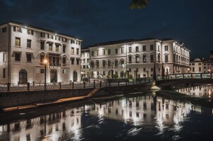 Um edifício histórico com vários andares, grandes janelas e uma ponte sobre um canal.