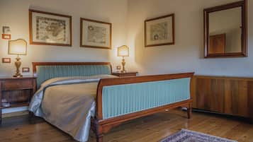 Quarto com cama de madeira, duas luminárias de cabeceira, mesa de cabeceira, cômoda e três mapas emoldurados na parede.