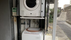 Máquina de lavar e secadora empilhadas verticalmente ao ar livre, com tubulações e painel de controle visíveis.