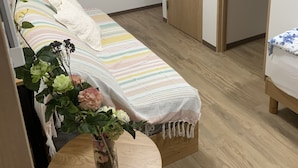 Quarto com uma cama, uma mesinha com um vaso de flores, uma porta e uma janela com cortinas.