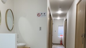 Corredor de hotel com pia branca, piso de madeira e placa de proibido fumar.