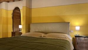 Uma cama com colcha verde, um guarda-roupa de madeira e duas luminárias de cabeceira num quarto com paredes amarelas e teto de madeira.