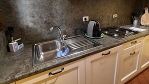 Cozinha com armários brancos, pia de aço inoxidável, fogão a gás e bancada com cafeteira.