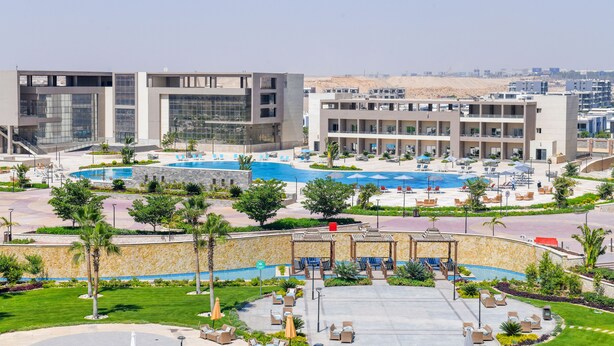 Um hotel moderno com piscina central, áreas de estar ao ar livre e um jardim paisagístico.