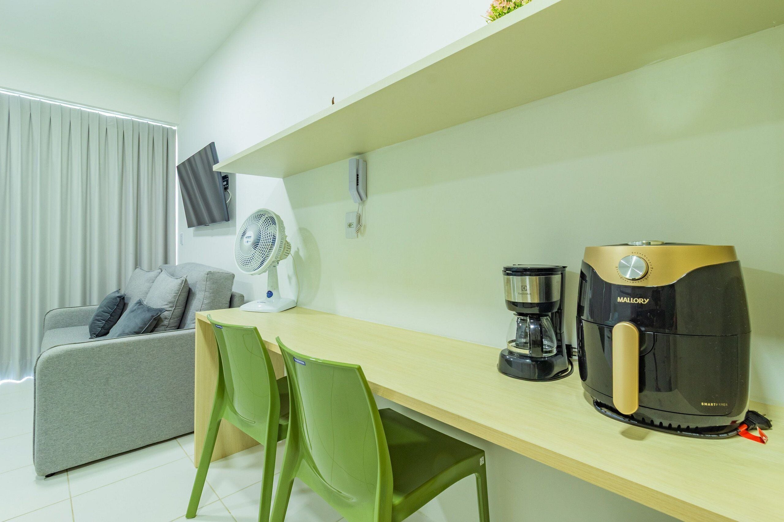 Uma kitchenette moderna com cafeteira, fritadeira elétrica e ventoinha na parede.