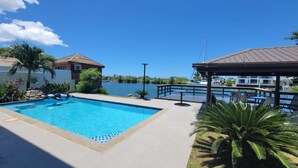 Piscina com vista para um corpo d'água, um gazebo e um edifício com telhado inclinado.