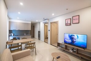 Uma sala de estar moderna com televisão de tela plana, mobiliário de madeira e uma área de cozinha ao fundo.
