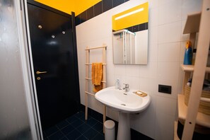 Um banheiro com porta preta, azulejos brancos, pia, espelho e porta-toalhas.