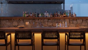 Uma área de bar com bancada de pedra, várias garrafas e cadeiras de vime.