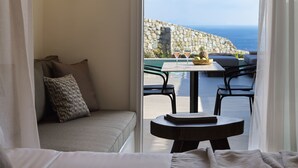 Varanda com vista para o oceano, parede de pedra e mesa com duas taças de vinho e uma tigela de fruta.