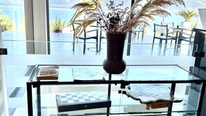 Uma mesa de vidro com um vaso de plantas secas, livros e uma bolsa rosa com a etiqueta 