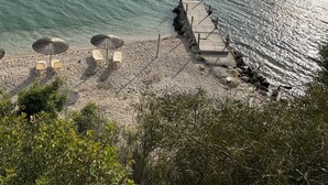 Uma praia com um píer de madeira que se estende até o mar, rodeada por águas cristalinas e montanhas ao longe.