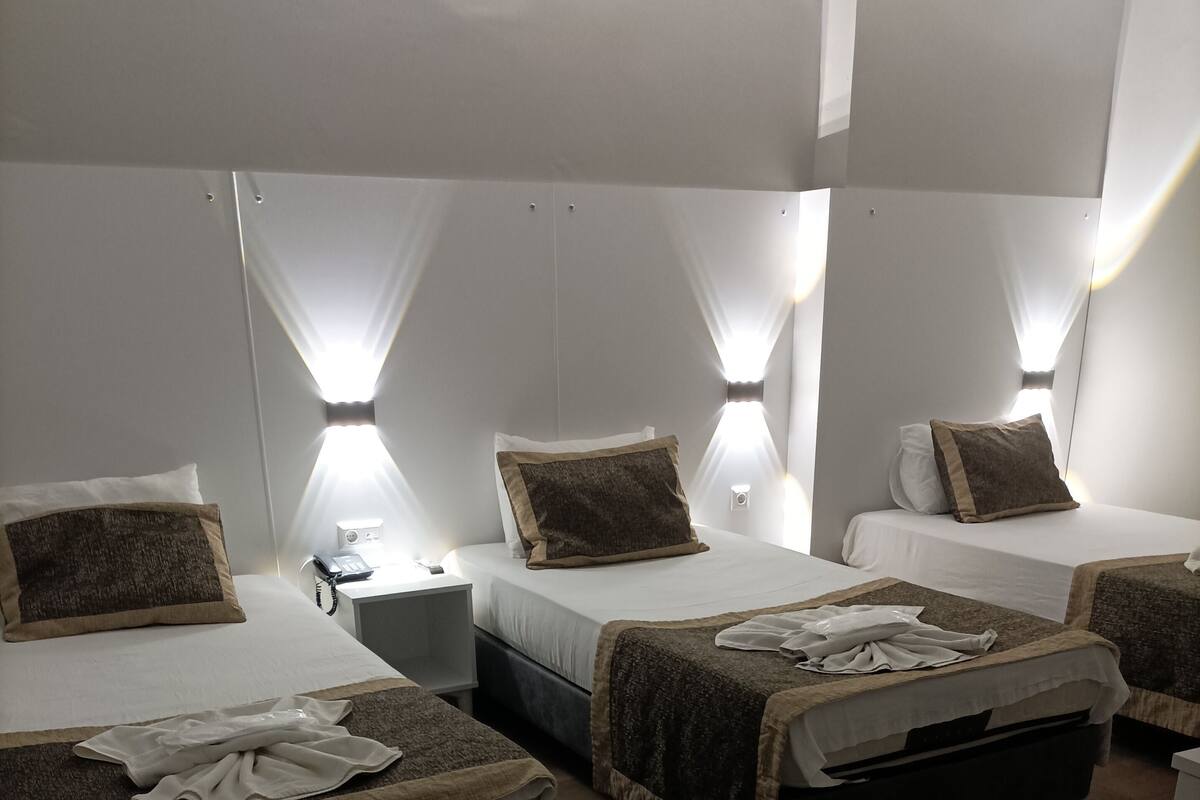 Quarto de hotel com duas camas, cada uma com travesseiro e cobertor, mesa de cabeceira com telefone e luminárias fixadas na parede.
