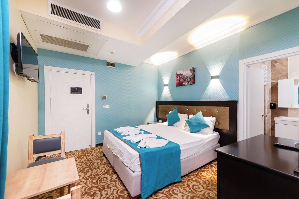 Quarto de hotel com uma cama, uma escrivaninha, uma cadeira, uma televisão na parede e um quadro na parede.