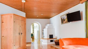 Uma sala de estar espaçosa com um armário de madeira, um sofá grande laranja, uma lareira e uma televisão fixada na parede.