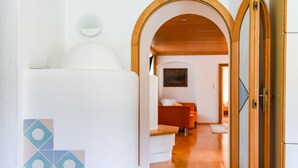 Um interior moderno com parede branca, azulejo estampado em padrão geométrico, porta de madeira e piso de madeira que levam a uma sala de estar com sofá e pintura.