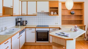 Cozinha moderna com armários brancos, máquina de café, chaleira e mesa de jantar de madeira com um banco.