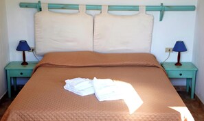 Uma cama com colcha marrom, dois travesseiros e uma pilha de toalhas brancas em uma cabeceira verde-água. Há duas mesas de cabeceira com abajures de cada lado da cama.